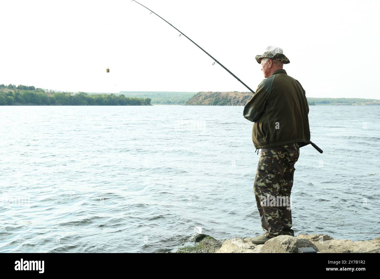 Fisherman with rod fishing near lake at summer, back view. Space for ...