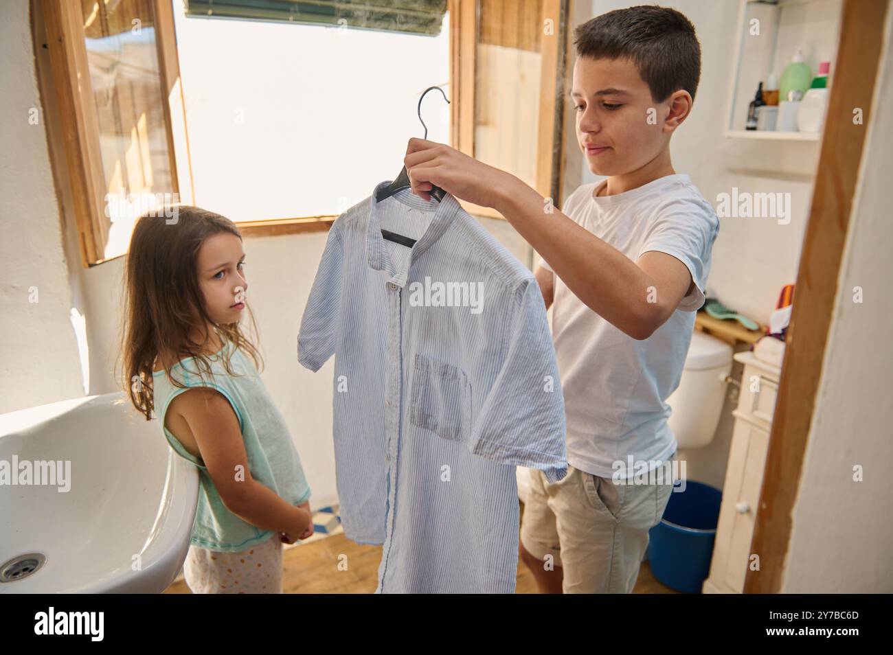 A young boy and his sister pick out clothes in a cozy room, showcasing ...