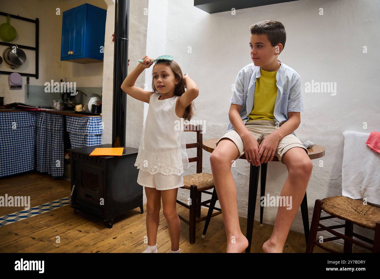 A young brother and sister share a playful moment in a cozy kitchen ...