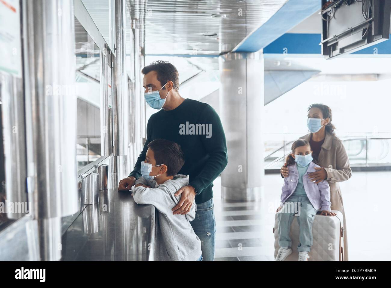 Family with two little kids in protective face masks buying tickets at ...