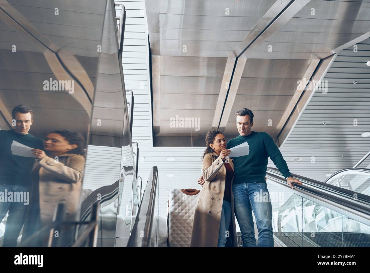 Mature couple carrying tickets while moving by escalator in airport ...