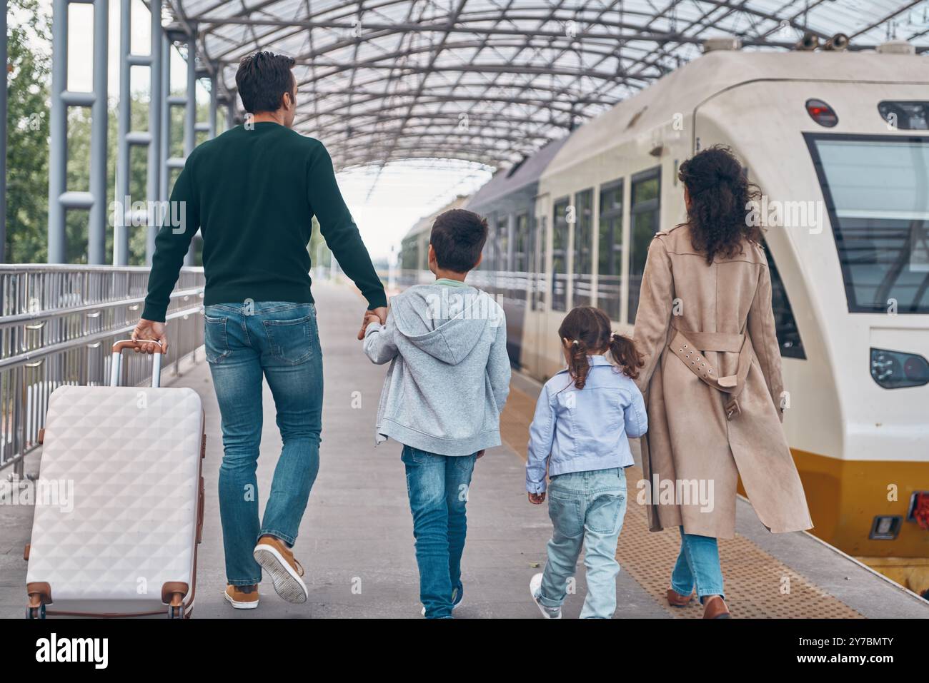 Rear view of family with two little kids walking by railroad station ...
