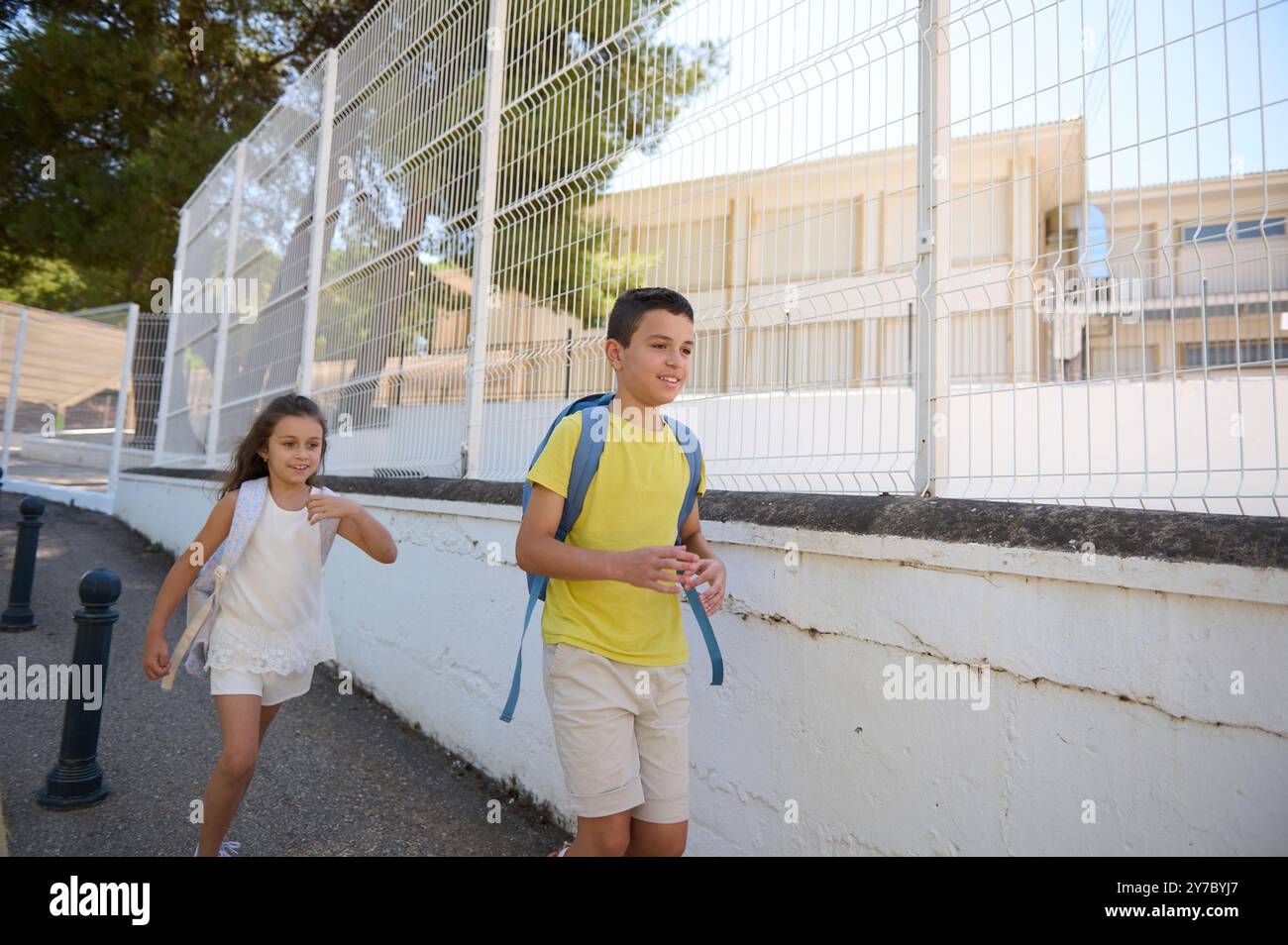 Two cheerful children with backpacks walking outside a school on a ...