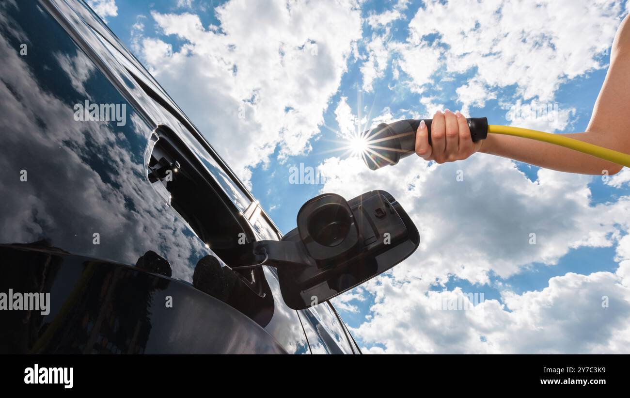Woman opening an electric car charging socket cap and plugging in a ...