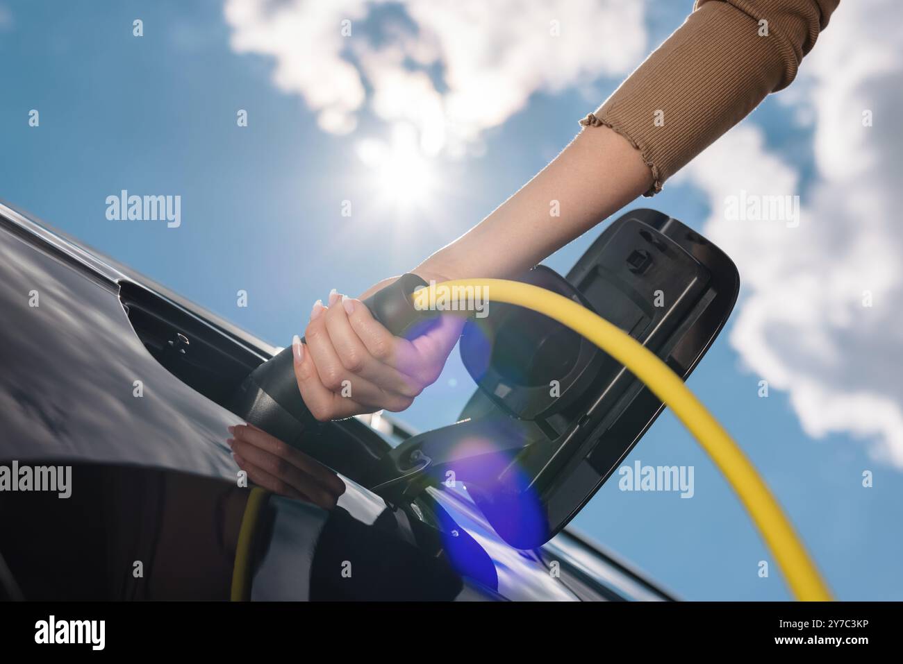 Woman opening an electric car charging socket cap and plugging in a ...