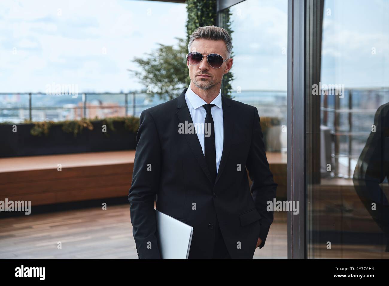 Confident mature man carrying laptop while walking on rooftop terrace ...