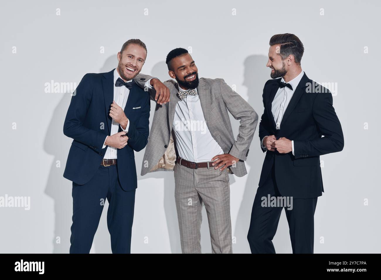 Three handsome young men in suits and bowties looking at camera and ...