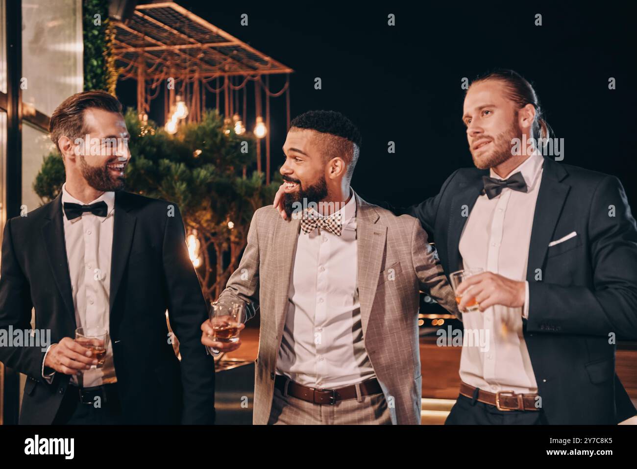 Three handsome men in suits enjoying whiskey and communicating while ...