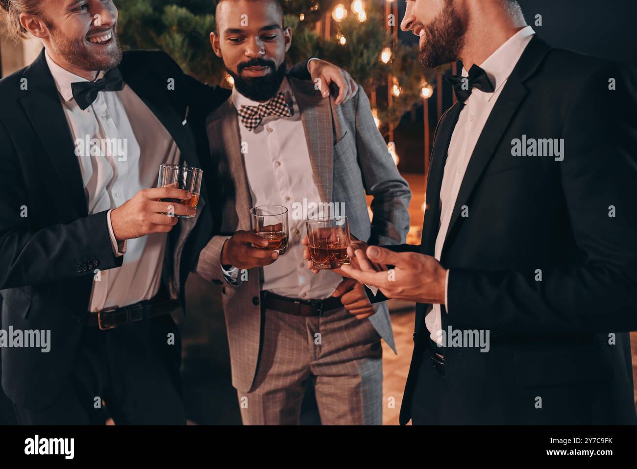 Three well-dressed men drinking whiskey and communicating while ...