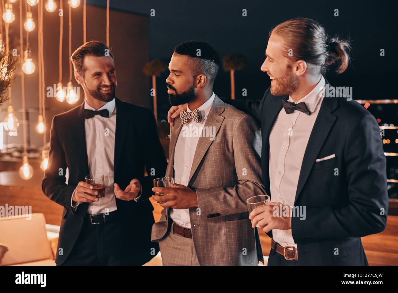 Three happy men in suits holding glasses with whiskey while spending ...
