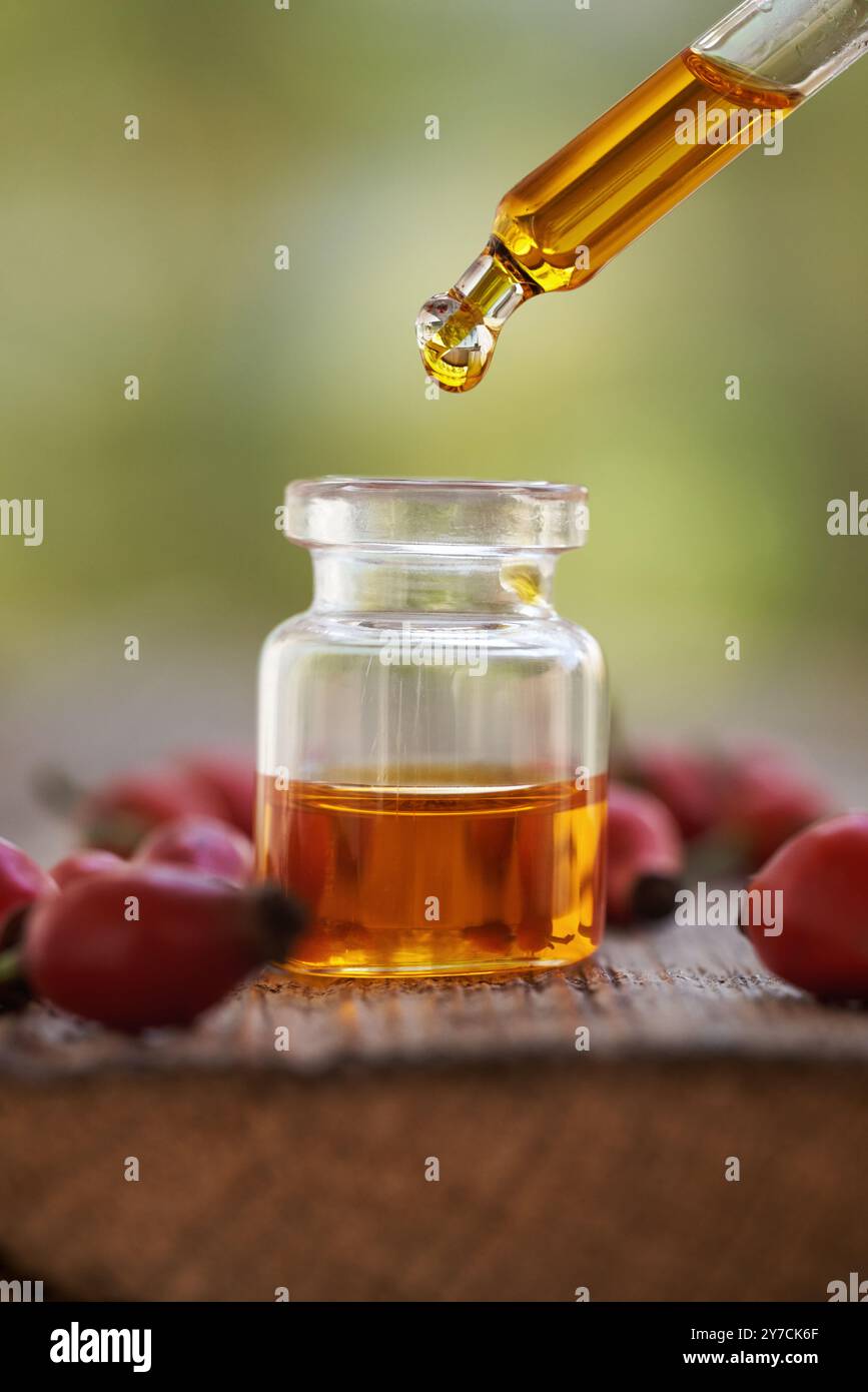 A bottle of rose hip seed oil with a drop falling from a pipette, with ...