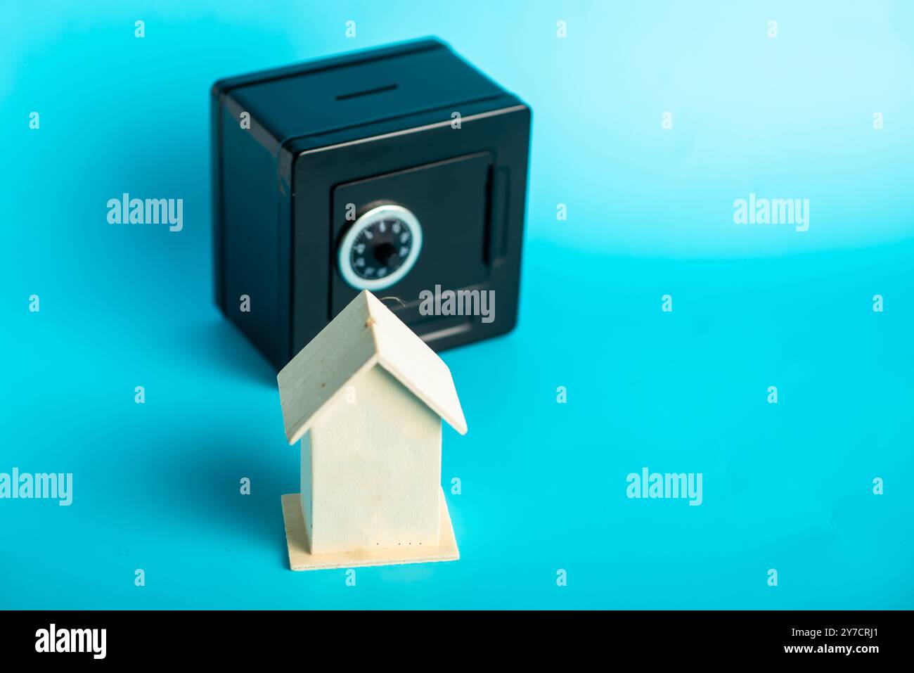 Secure savings: small wooden house and mini safe on blue background ...
