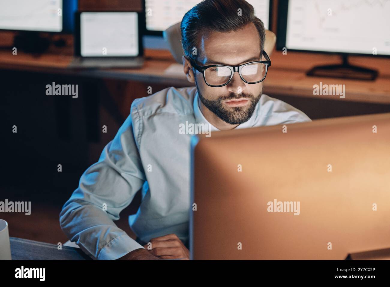 Concentrated young man working on computer while staying late in the ...