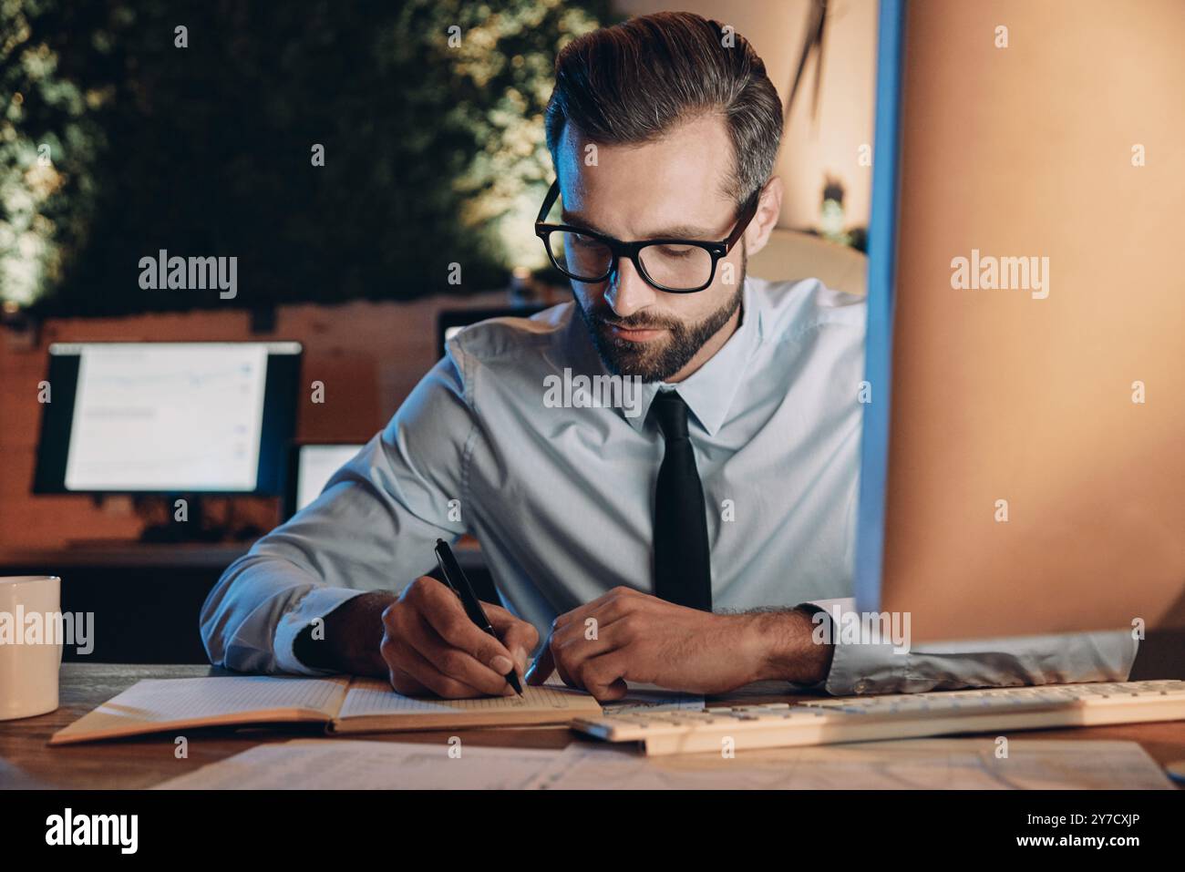 Confident young man making notes while staying late in the office Stock ...