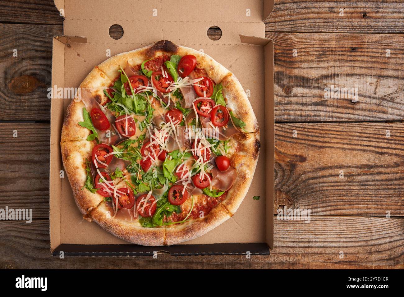 Whole pizza in a cardboard on a rustic wooden board with copyspace ...