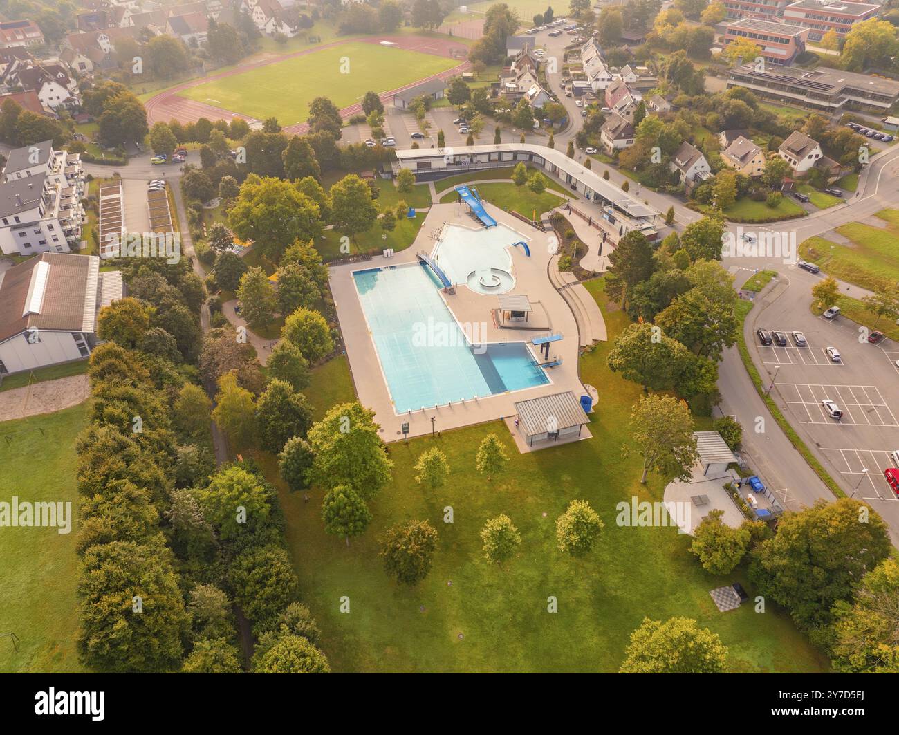 A swimming pool with outdoor area, surrounded by green spaces and trees ...