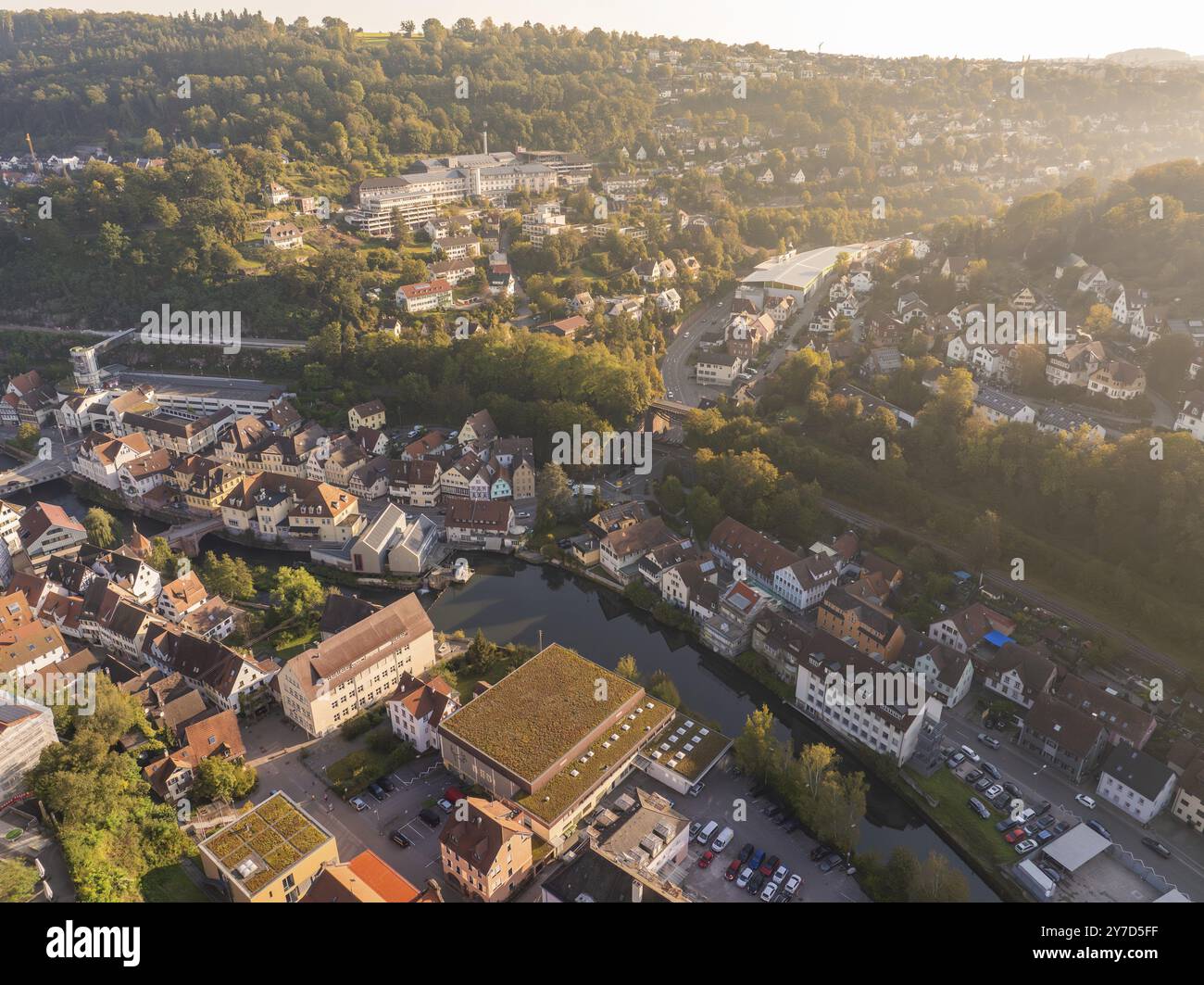 Aerial view of a town surrounded by green hills and a river, with many ...