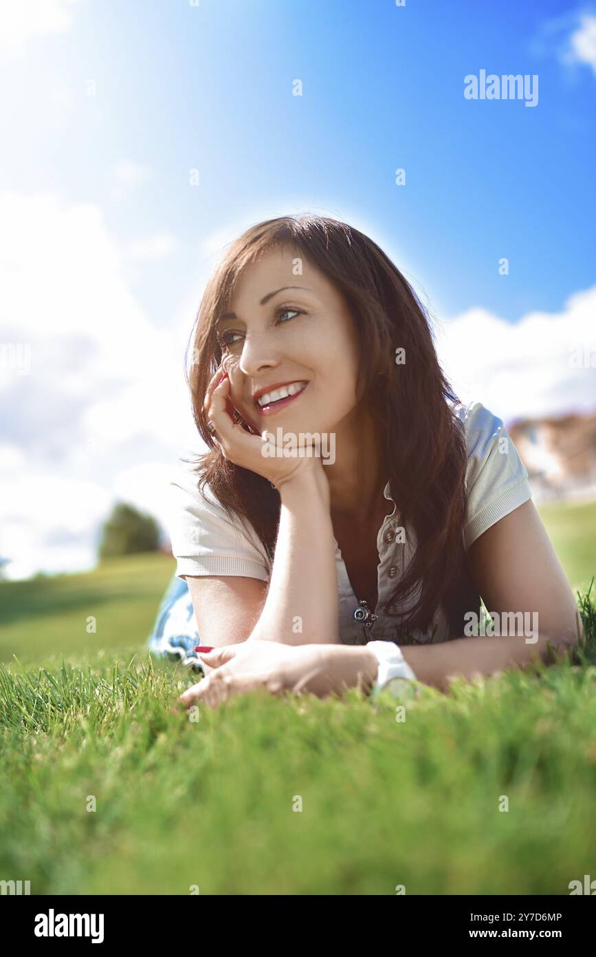 Summer-vacation, adult woman relaxed lying on green grass in an outdoor ...