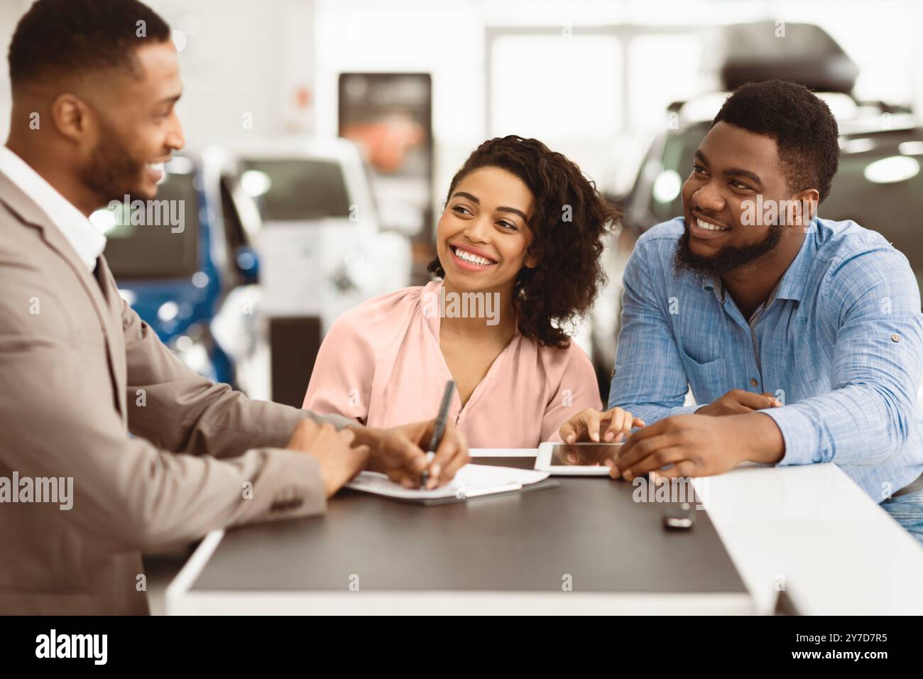 African Couple Signing Papers With Salesman Standing In Dealership ...
