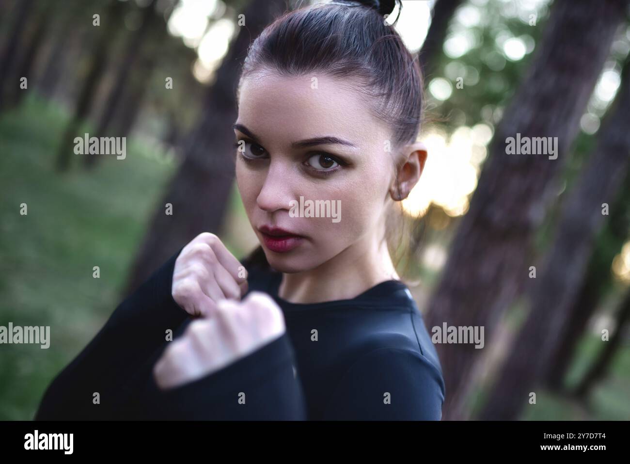 Young woman doing martial arts training in sporty black top holding hands in fighting pose ...