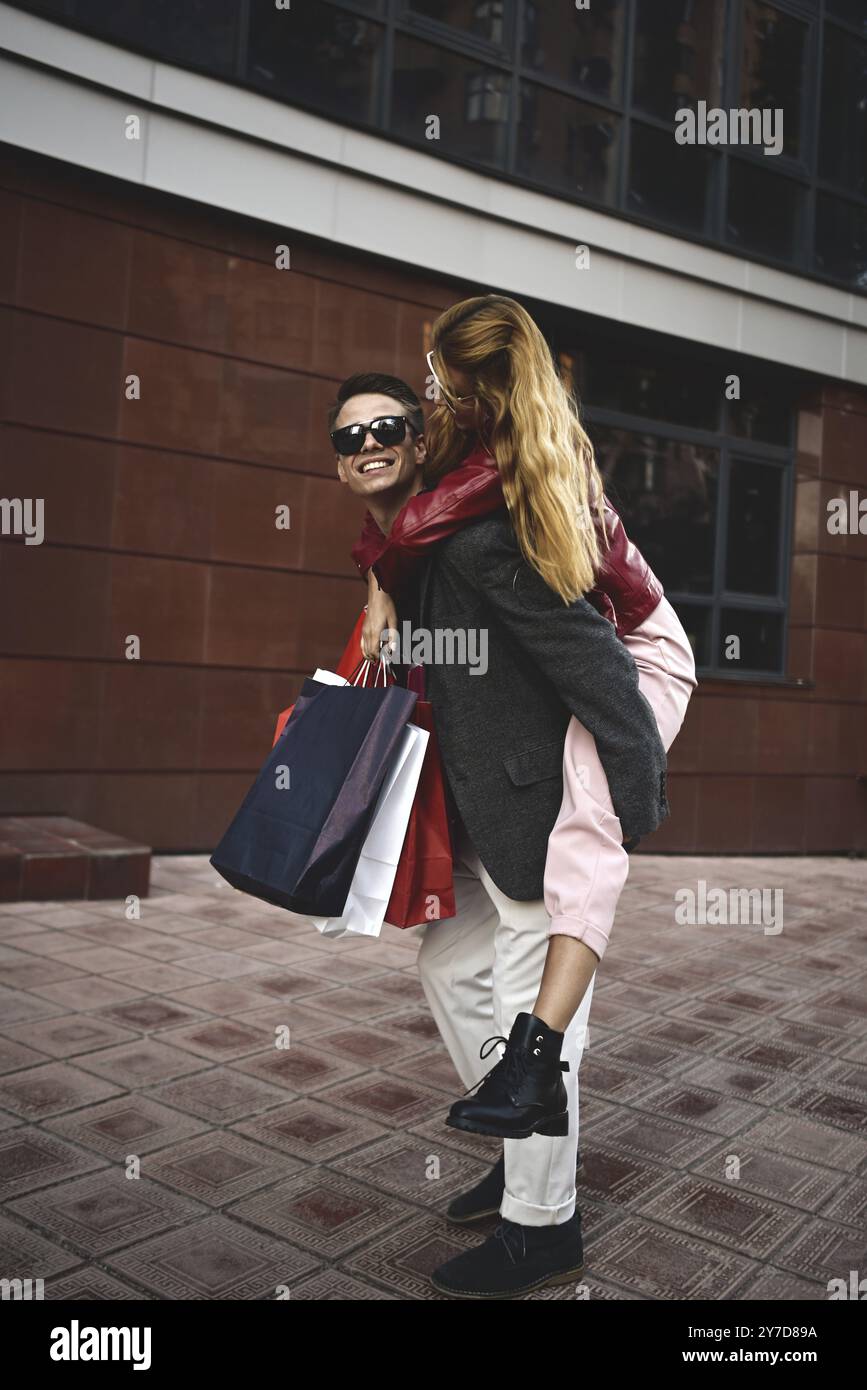 Happy couple shopping together and having fun. Boyfriend carrying his ...