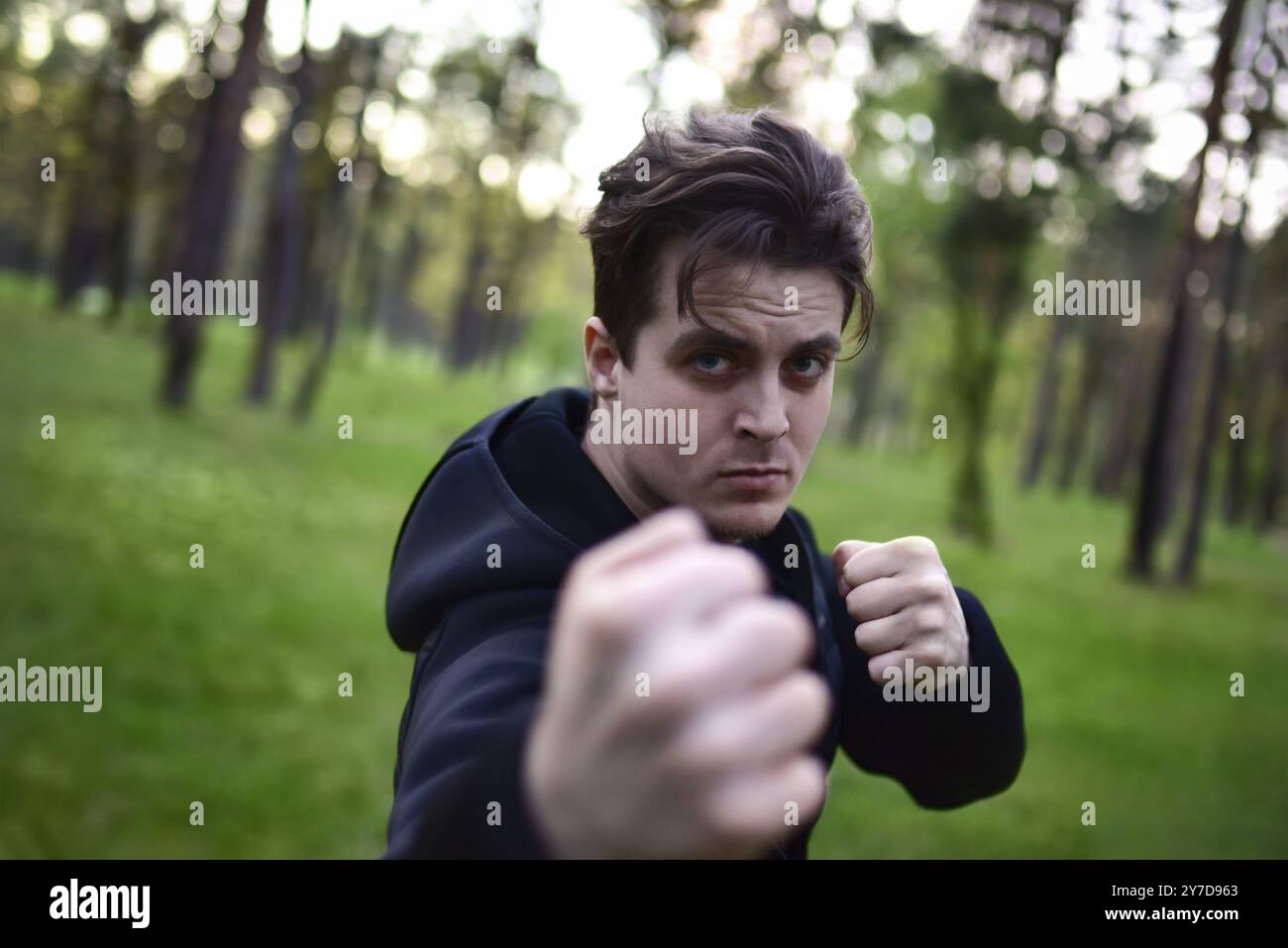 Sporty young man in a sporty black jacket in a fighting pose raising ...