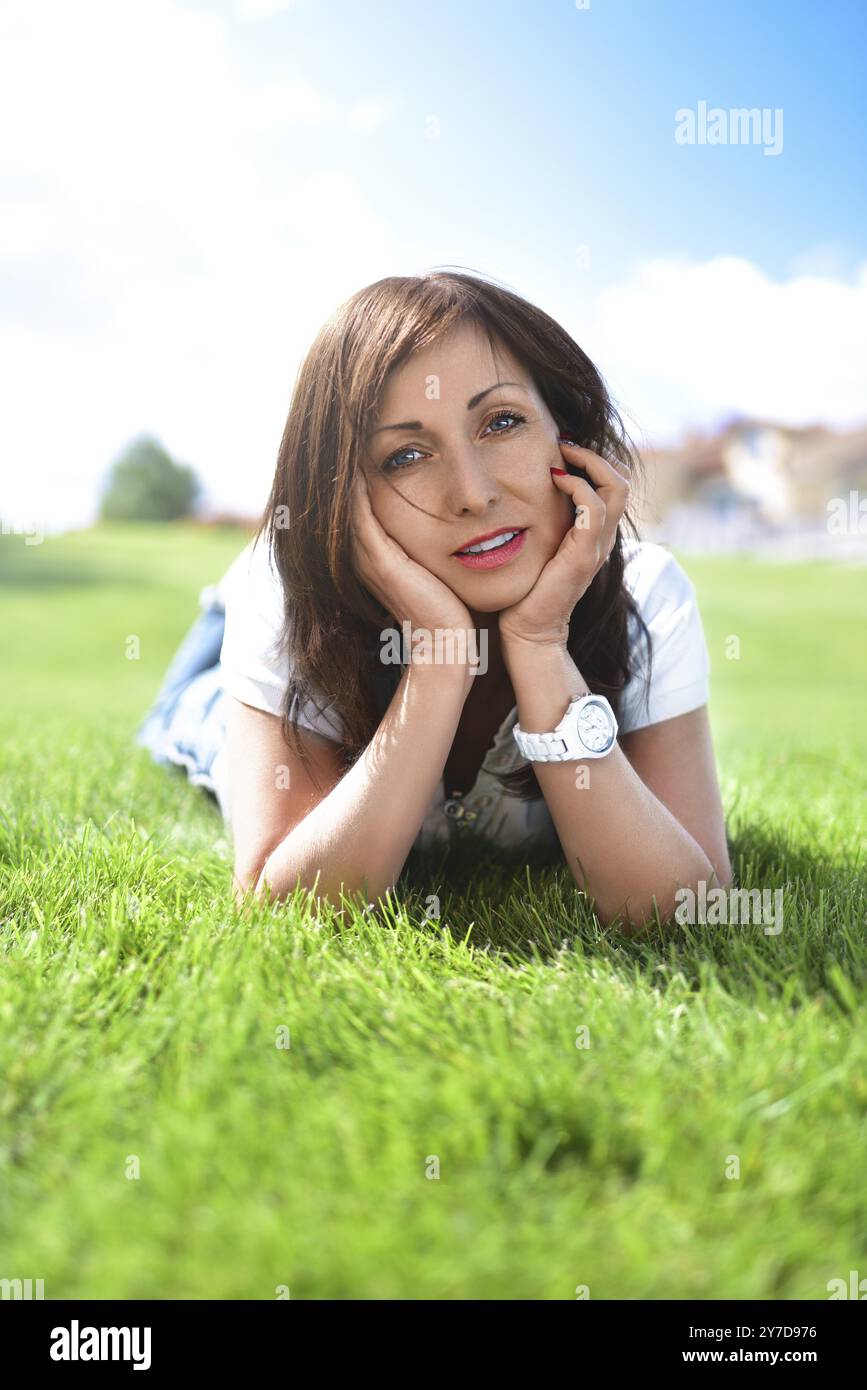 Summer-vacation, adult woman relaxed lying on green grass in an outdoor ...