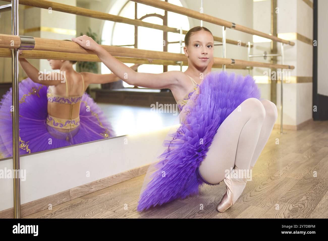 Young attractive ballerina is crouching at bar in ballet class in ready ...