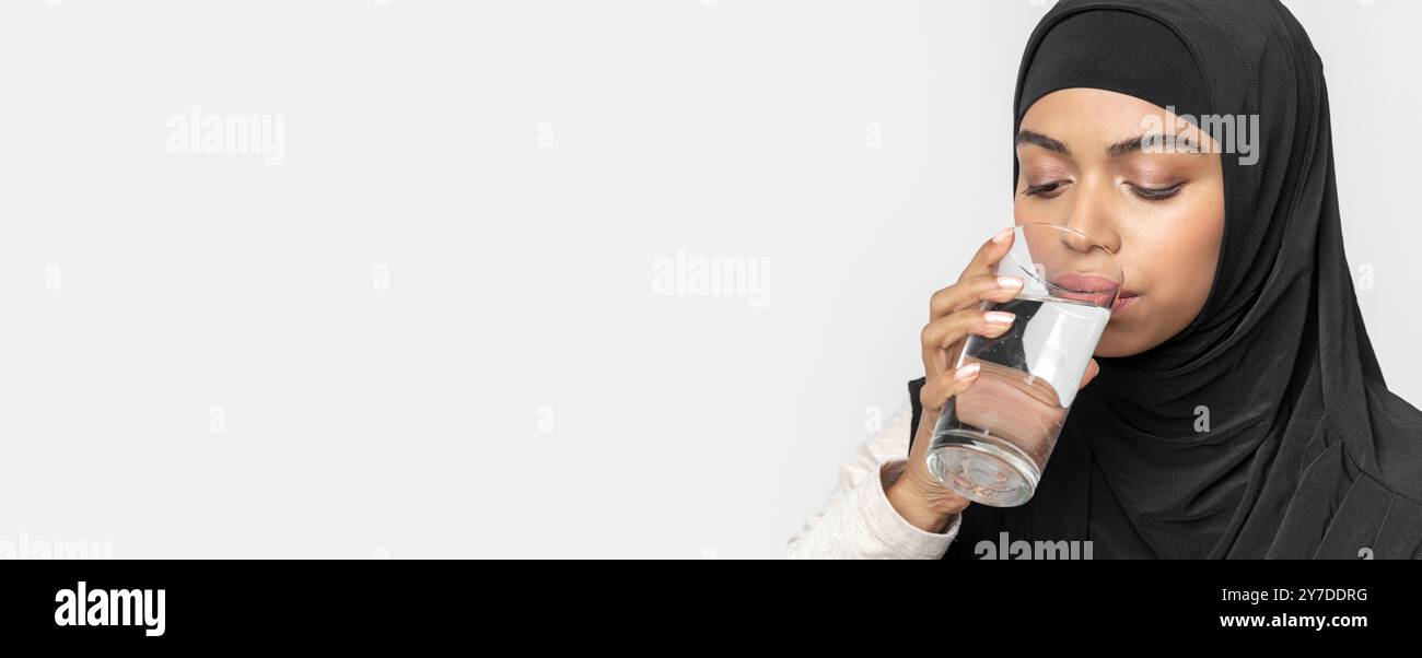 Thirsty black muslim woman in hijab drinking mineral water from glass Stock Photo - Alamy