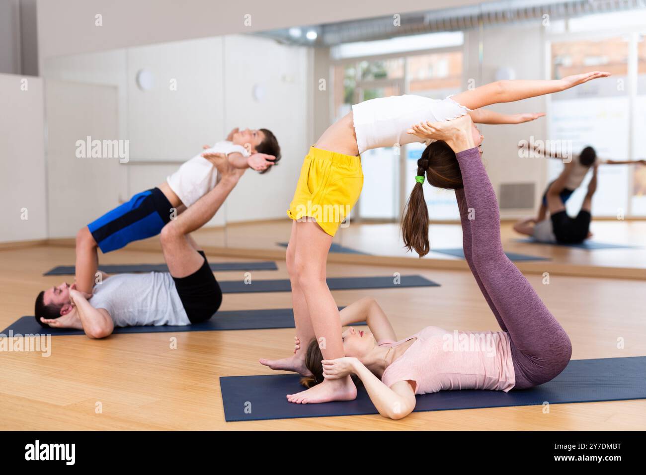 Tween girl with mother doing exercises in pair during family yoga ...