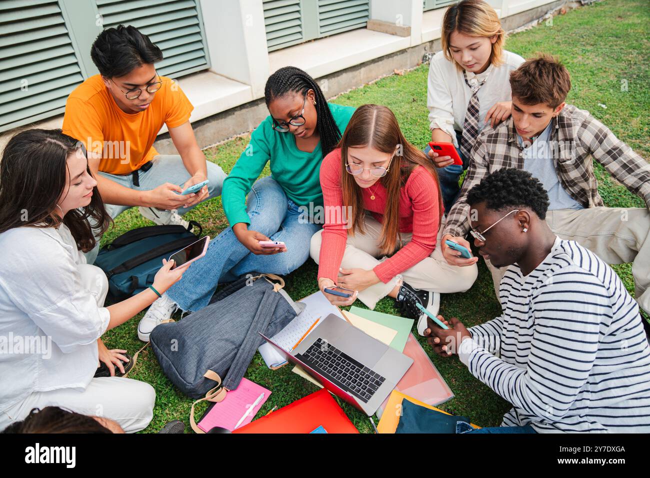 Diverse group of students sitting on the university campus lawn, using ...