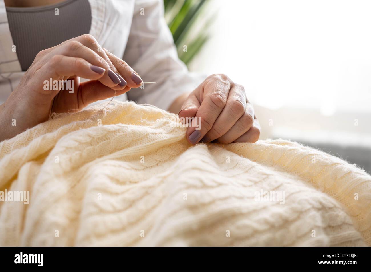 Clothes repair concept. A woman uses her hands to sew up a hole in a ...