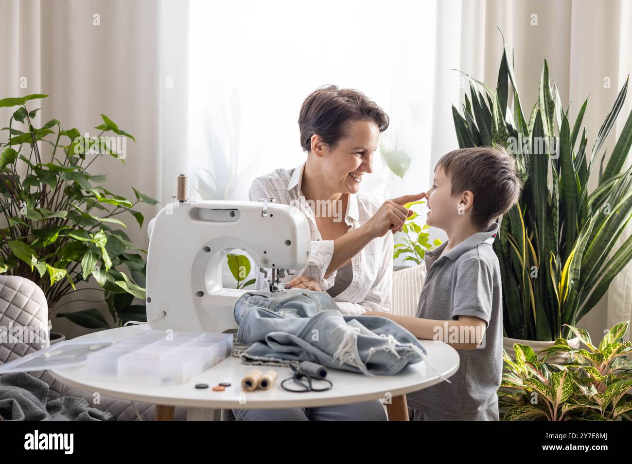 Mom and son are repairing old torn jeans using a sewing machine. A ...