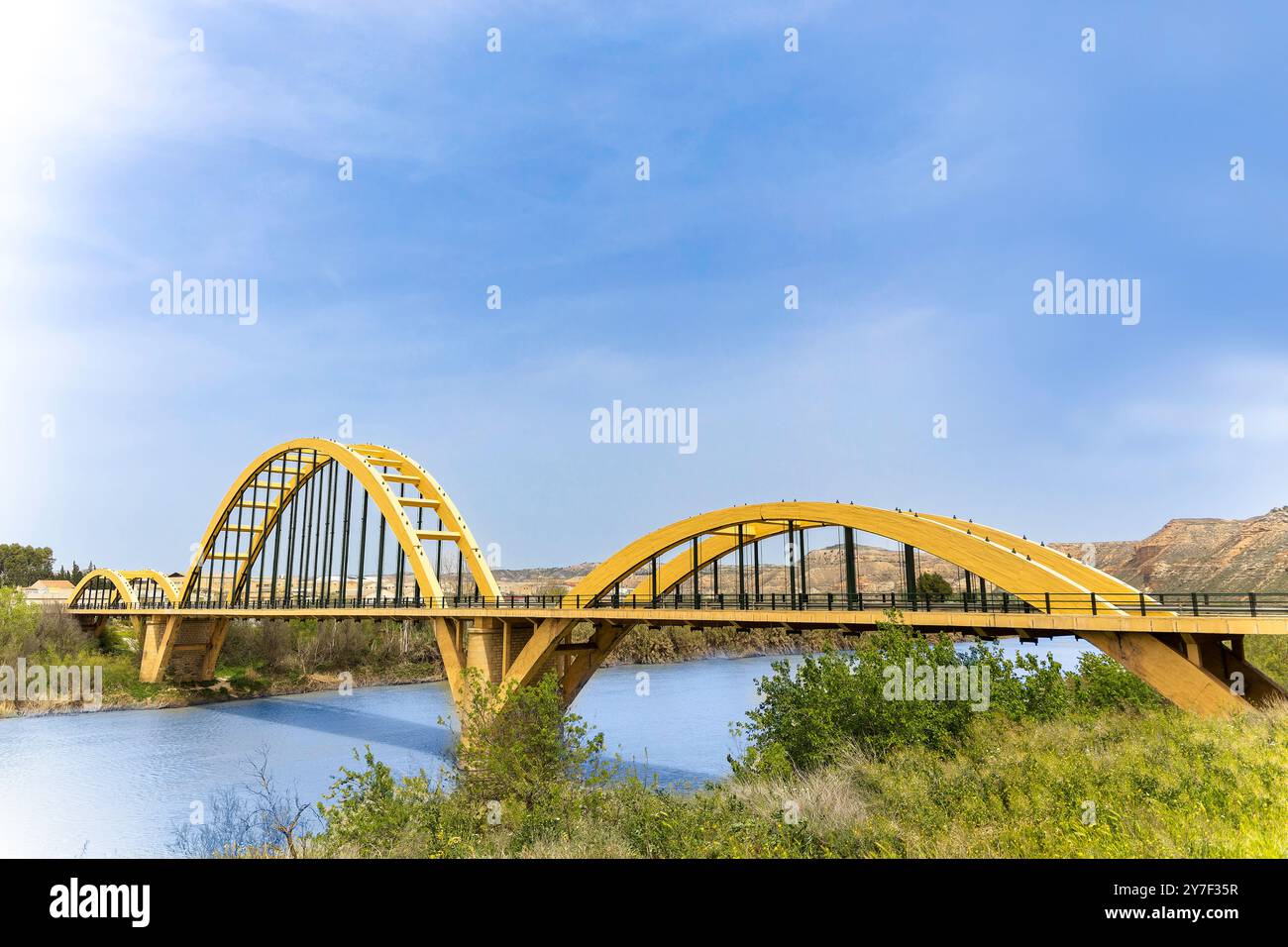 A yellow bridge spans a river, with a clear blue sky above. The bridge ...