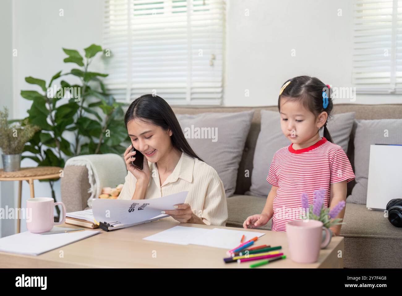 Focused Mother Balancing Professional Tasks While Daughter Observes ...