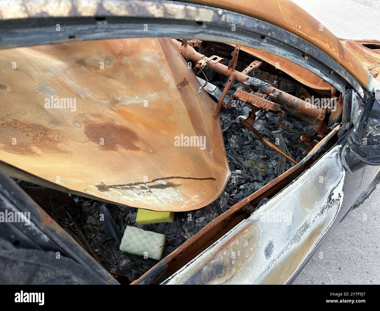 The charred remains of a car interior after a fire. The metal is rusted ...