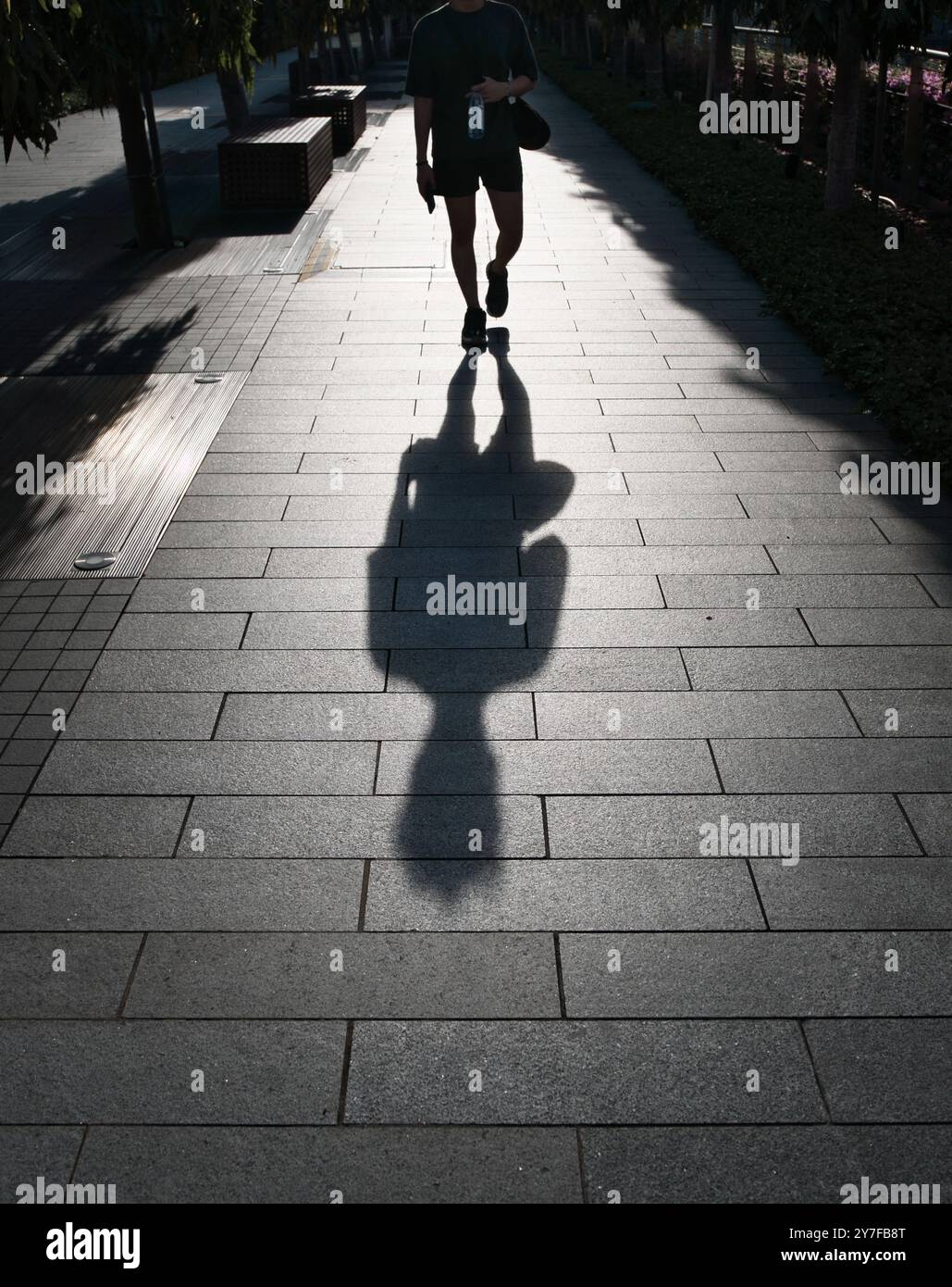Shadow of man walking on walkway in city. Backlit and in silhouette ...