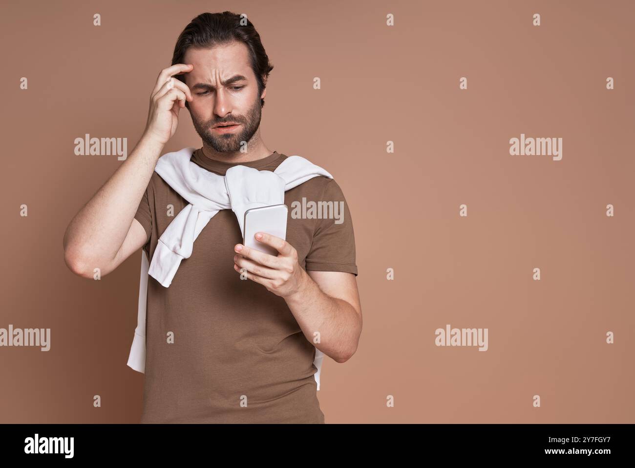 Frustrated young man looking at smart phone while standing against ...