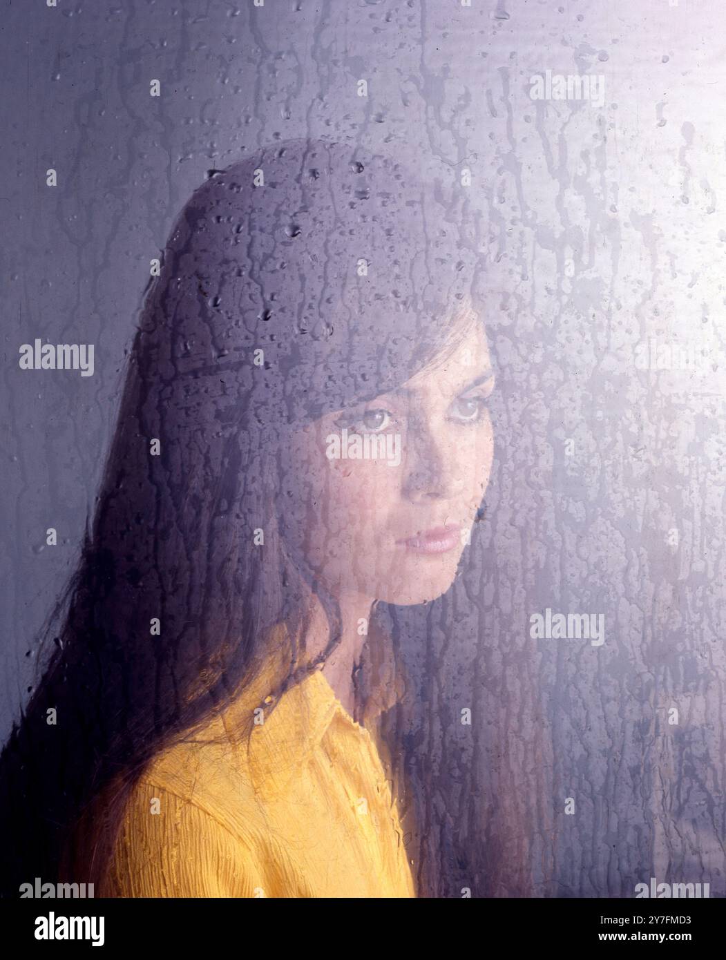 A young woman looking through a rain streaked window 1970's Stock Photo ...