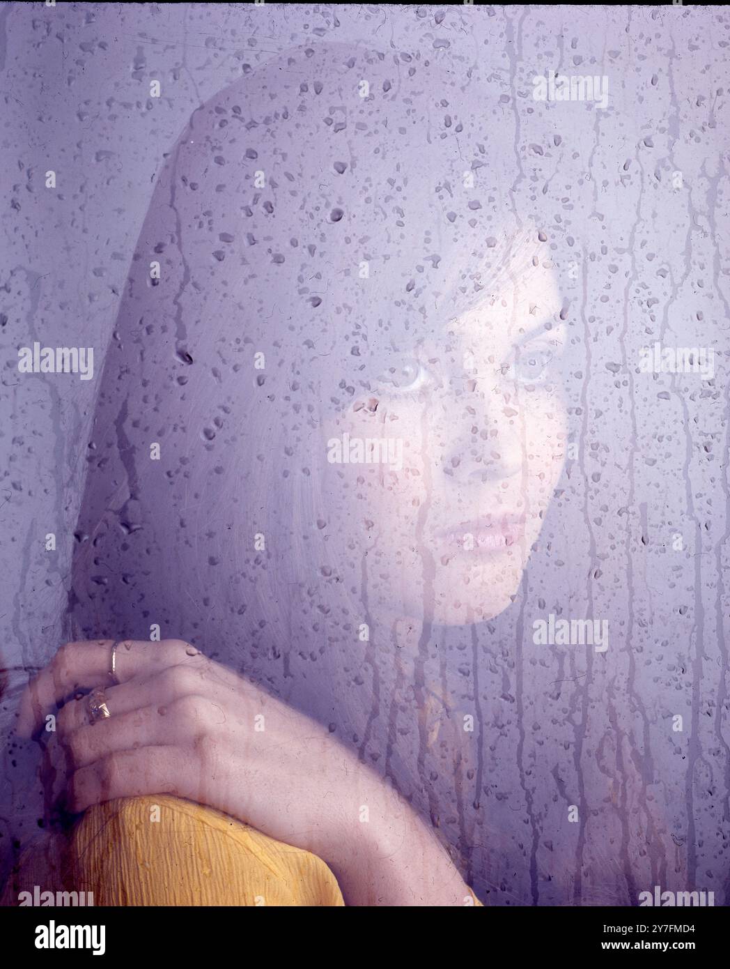 A young woman looking through a rain streaked window 1970's Stock Photo ...