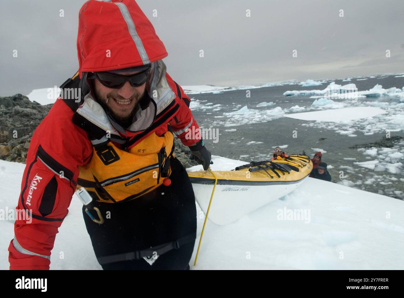 A man hauls a kayak up a steep ice embankment in the west coast of ...
