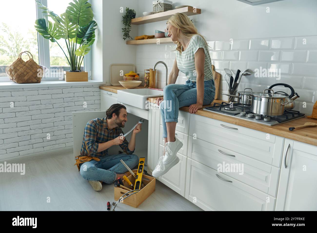 Confident young man repairing a sink while woman sitting on the kitchen ...