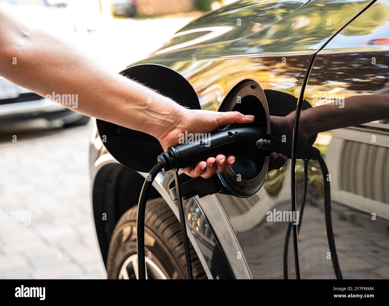 Close up of arm plugging EV charger into electric vehicle outside Stock ...