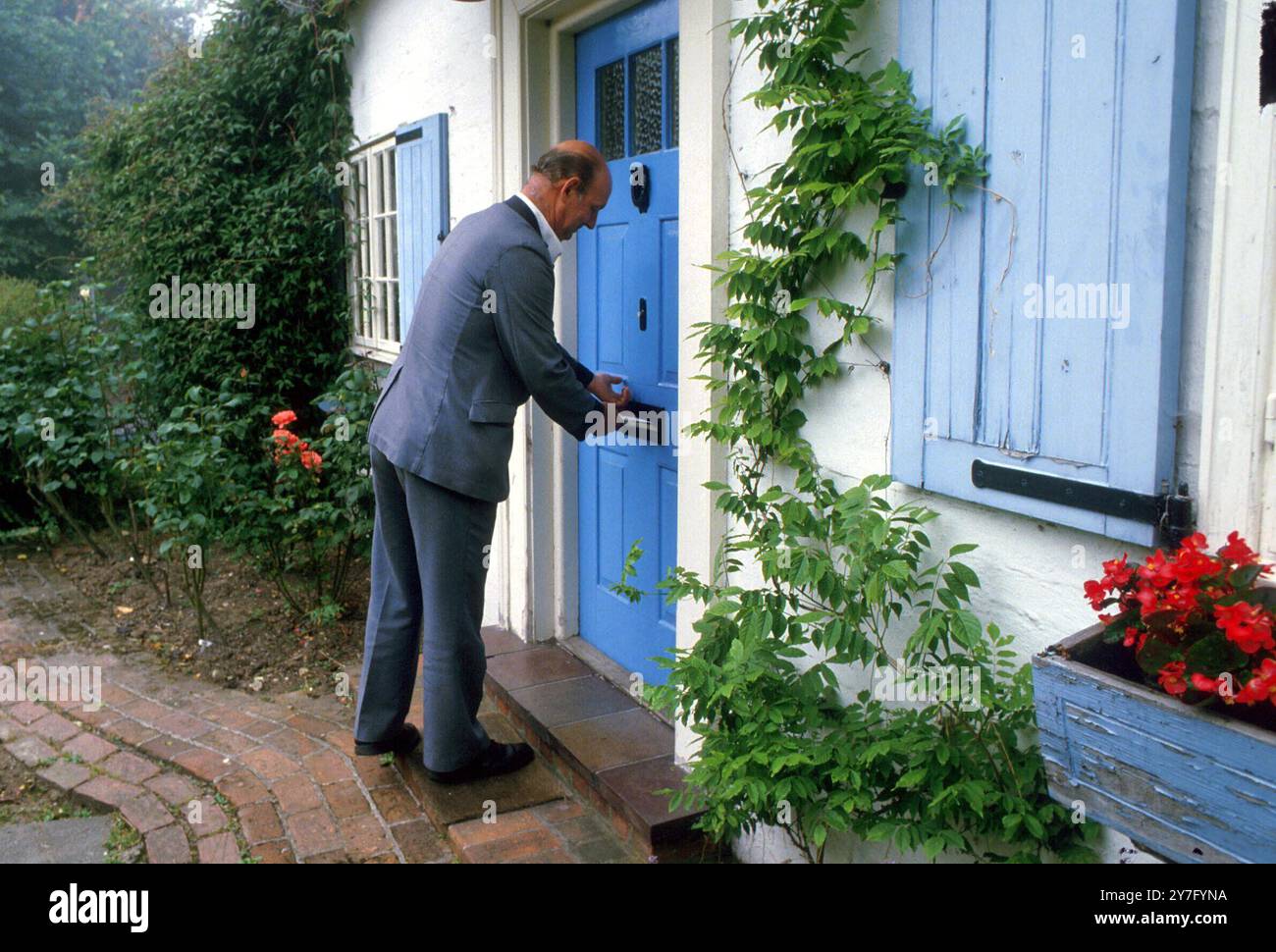 Man posting letters through letterbox in front door Stock Photo - Alamy