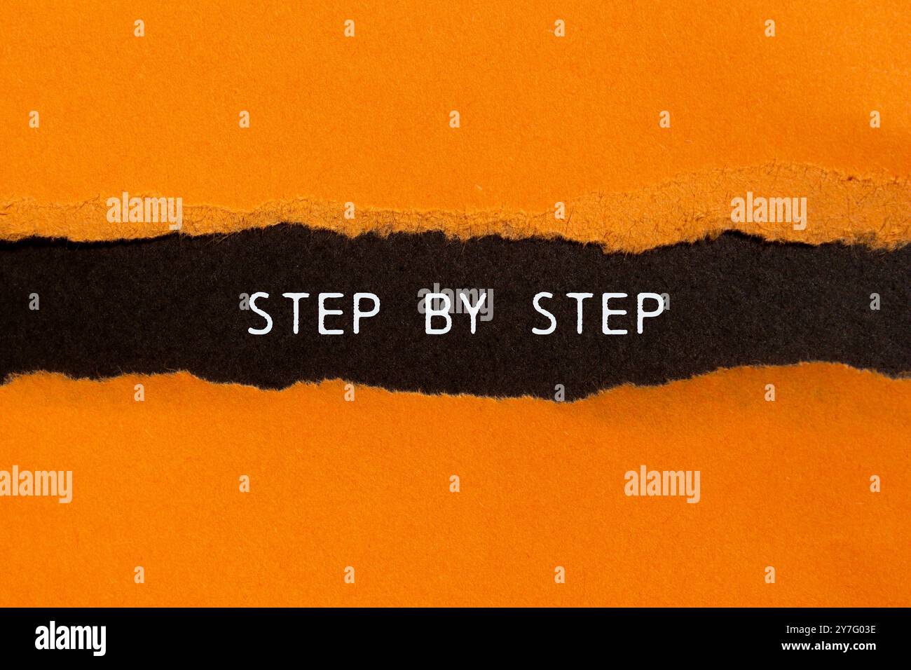 Step by step message written on ripped torn orange paper on black ...
