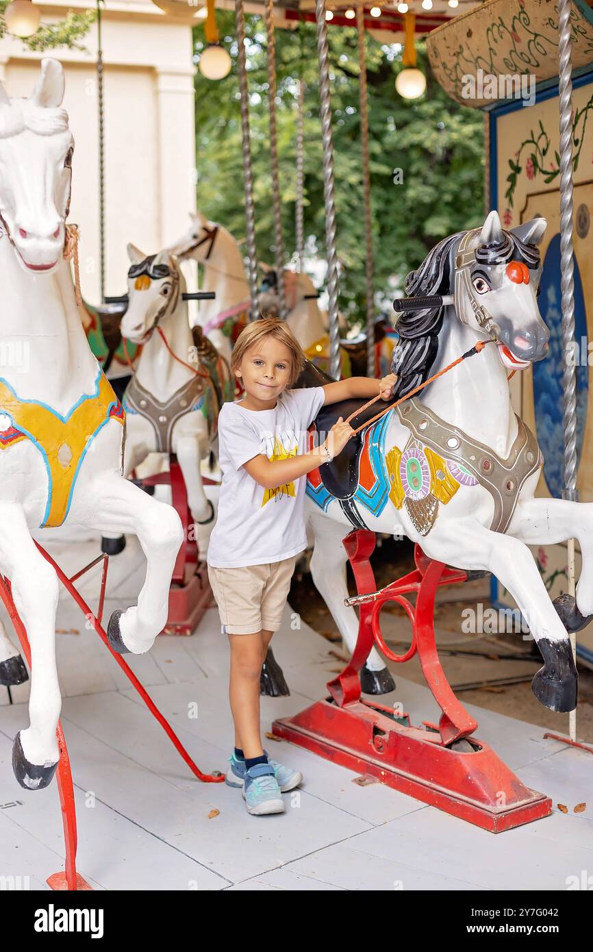 Cute blond child, going on Merry Go Round, kid play on carousel park ...