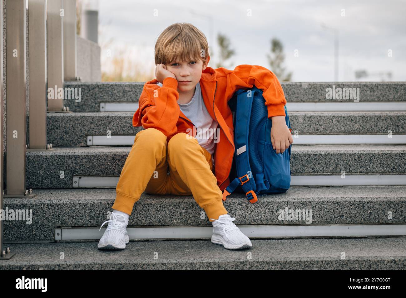 Little boy, schoolboy, with a backpack sits on the stairs and is sad ...