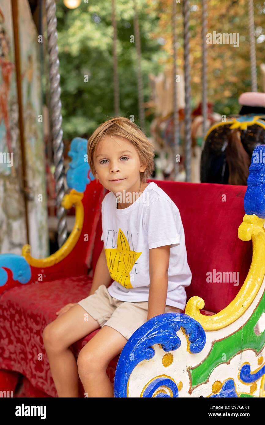 Cute blond child, going on Merry Go Round, kid play on carousel park ...
