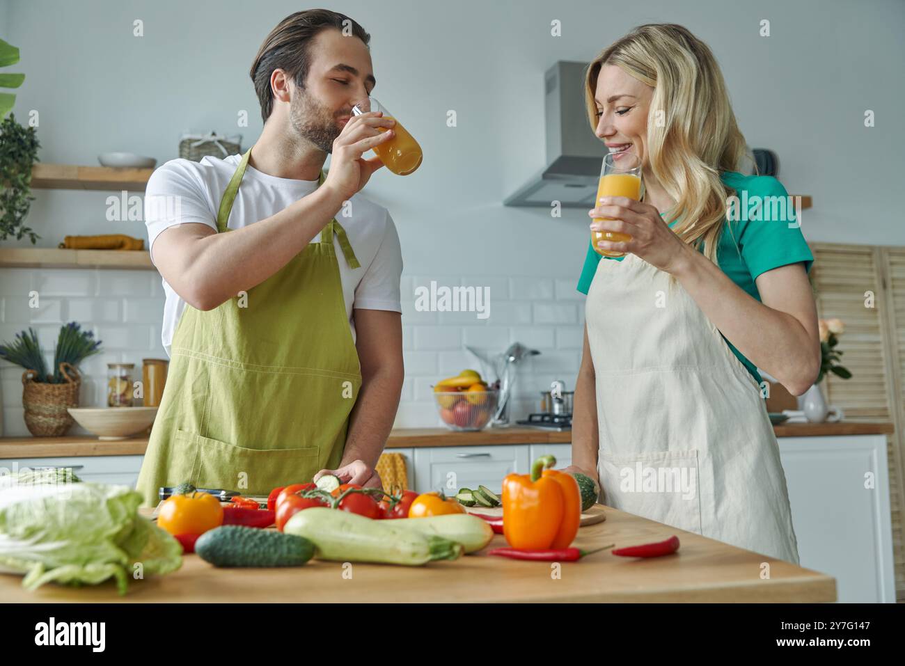 Happy couple drinking orange juice and smiling while cooking at the ...