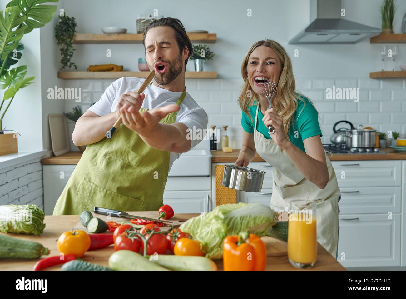 Playful couple having fun and singing while cooking together at the ...
